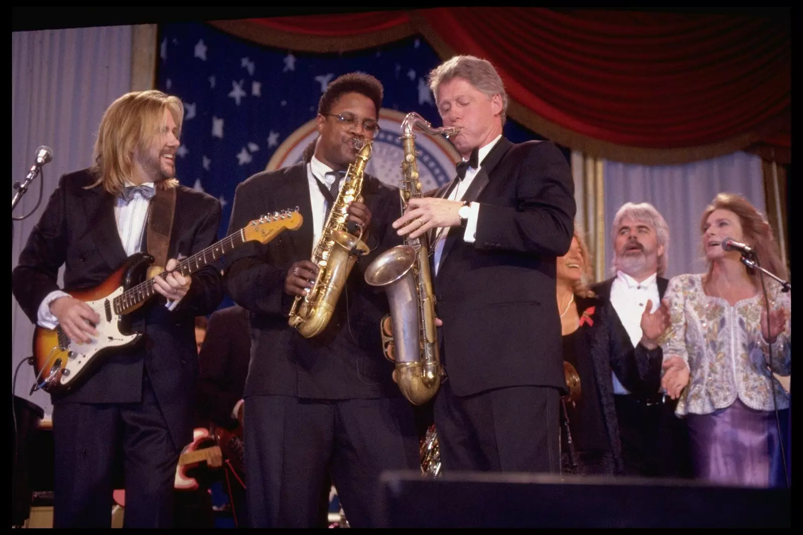 Bill Clinton spelar saxofon med musiker på scenen med Kenny Rogers och Judy Collins bakom sig under DC Armory...