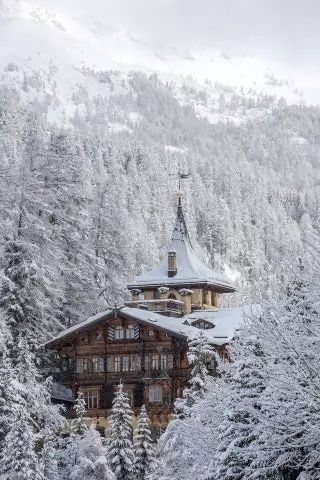 Una casa cubierta de nieve que se asoma entre los árboles.