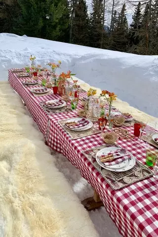 E Schwäizer Picknick vu roude Gingham a Pelz op engem Mëttegiessen Dësch am Schnéi ausgegruewen.